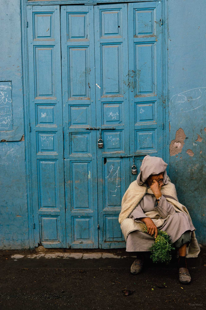 Man Holding Greens Sitting Against Blue Paneled Door, Marrakech – Jay Maisel